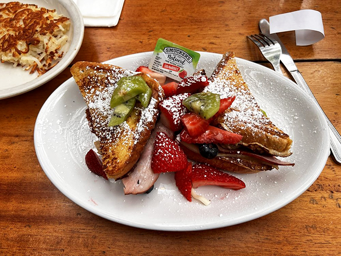 French toast transformed into a Monte Cristo sandwich, dusted with powdered sugar and fresh fruit—breakfast and dessert having a delicious identity crisis.