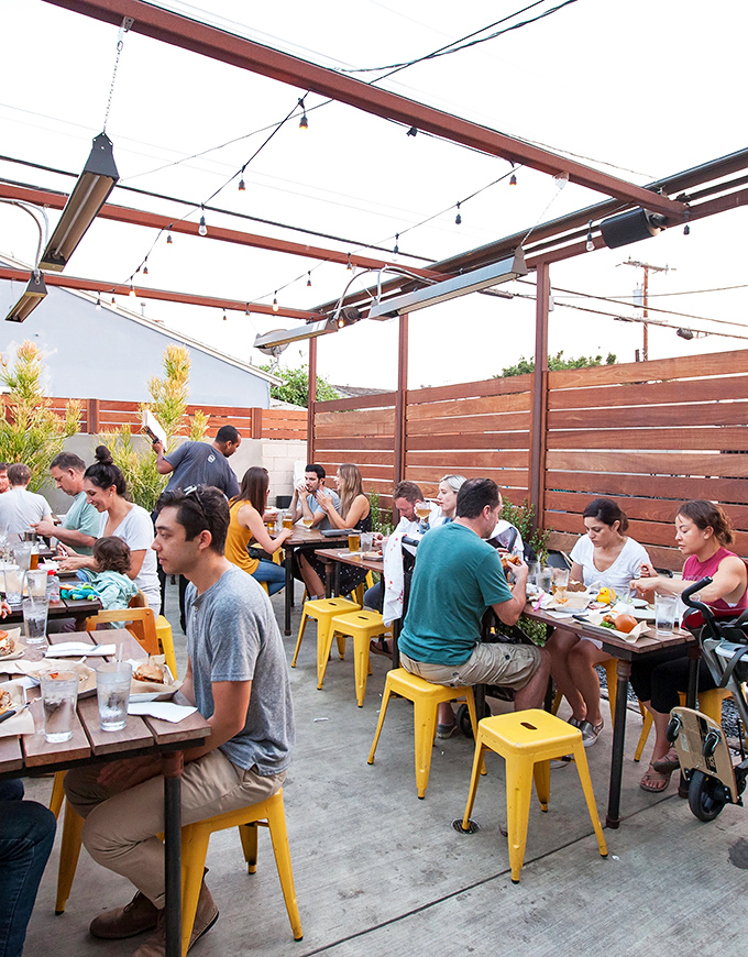 The outdoor patio doesn't just seat diners—it hosts food pilgrimages. Those yellow stools collect people who've come to worship at the altar of perfect fries.