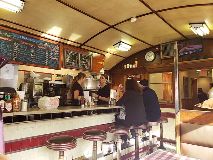 The curved ceiling of the original diner car frames the counter where magic happens—servers and cooks working in the practiced rhythm of diner perfection.