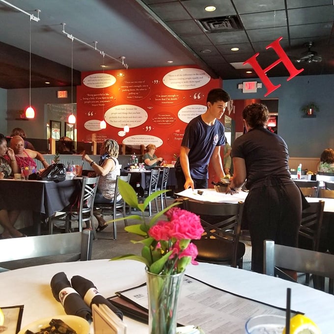 A vibrant red wall showcases inspirational quotes while diners and staff create their own memorable moments. Fresh flowers on each table—a small touch that speaks volumes.
