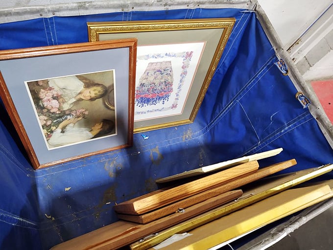 Framed memories and mass-produced art share space in the blue bins—someone's once-cherished wall décor awaiting resurrection in a new home.