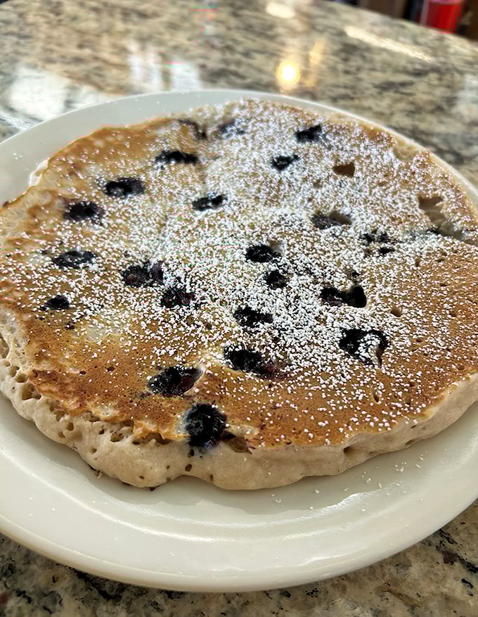 Blueberry pancakes with the perfect distribution of fruit—like edible polka dots on a golden breakfast canvas. Powdered sugar adds the finishing touch.