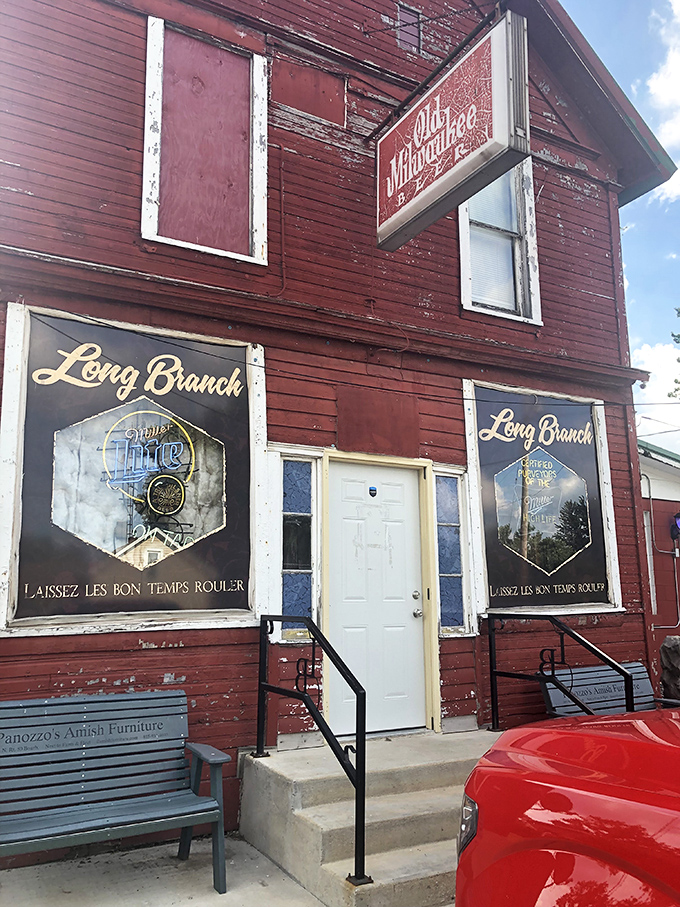 Entrance of a rustic red building labeled "Long Branch," with twin signs featuring a beer logo and the phrase "Laissez Les Bon Temps Rouler," accessed by concrete steps with black railings on either side. 