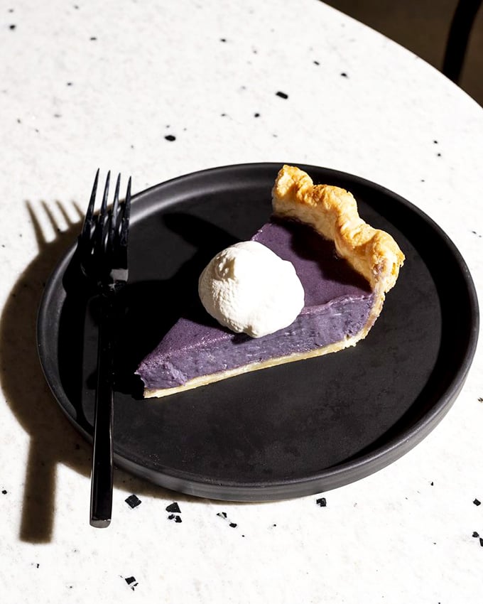 This slice of purple pie isn't just dessert, it's a conversation piece—its vibrant hue and perfect dollop of cream suggesting the kitchen isn't afraid of bold choices.
