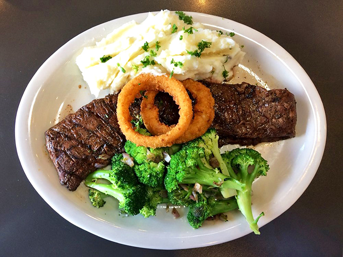 A steak that's lived an interesting life, now resting gloriously beside fluffy mashed potatoes and crisp onion rings—the holy trinity of diner perfection.