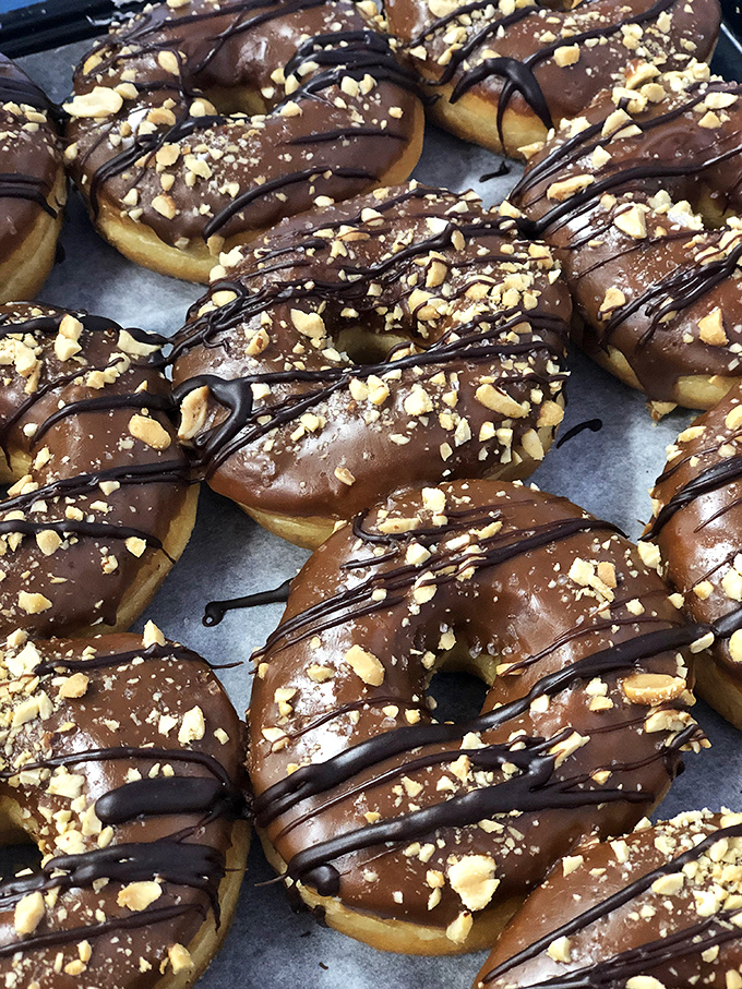 Chocolate-glazed donuts with peanuts and chocolate drizzle – proof that sometimes more is more, especially when it comes to toppings.