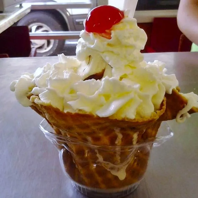 This isn't just ice cream—it's a tower of sweet nostalgia crowned with whipped cream and a cherry, served in a waffle cone throne.