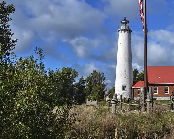 The Tawas Point Lighthouse stands sentinel over Lake Huron, its whitewashed tower a beacon of maritime history against Michigan's moody skies.