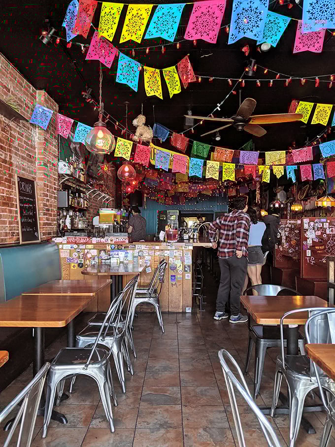 Papel picado flags create a perpetual fiesta overhead while exposed brick walls ground the space in urban cool. This isn't decoration—it's a mood.