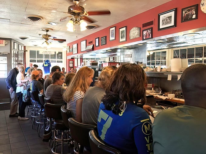 Counter seating isn't just practical—it's theater with a front-row view of breakfast artistry in action. The red walls and ceiling fans create classic diner ambiance.