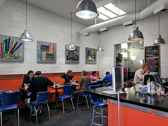 Inside, bright orange booths pop against white walls adorned with colorful artwork – where industrial-chic meets retro diner comfort in perfect harmony.