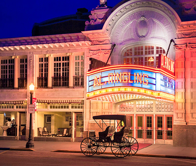 The Al. Ringling Theatre glows at night like a jewel box of entertainment, complete with horse-drawn carriage—because Ubers were scarce in 1915.