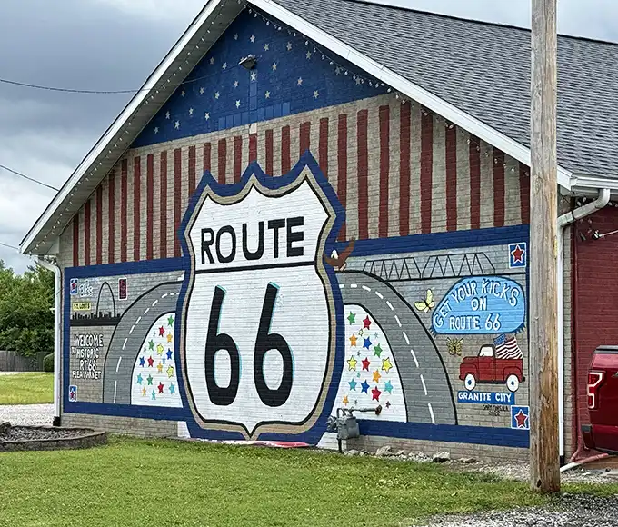 This patriotic Route 66 mural isn't just wall art—it's a siren call to road trip enthusiasts and nostalgia seekers.