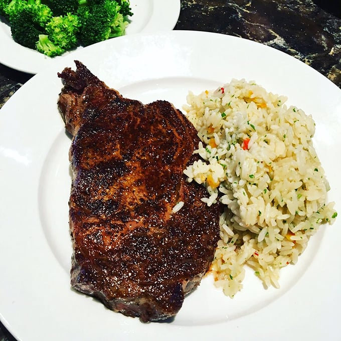 This 12oz ribeye doesn't just sit on the plate—it commands attention with its perfect char and juicy interior, flanked by rice pilaf and broccoli for those with a conscience.