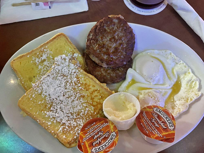 French toast dusted with powdered sugar alongside savory sausage patties and perfectly cooked eggs – breakfast harmony on a plate.