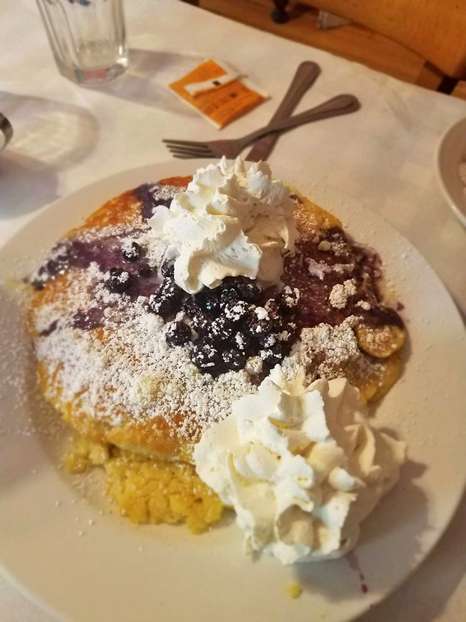 Blueberry pancakes crowned with clouds of whipped cream—proof that sometimes the best things in life require both a fork and napkin.