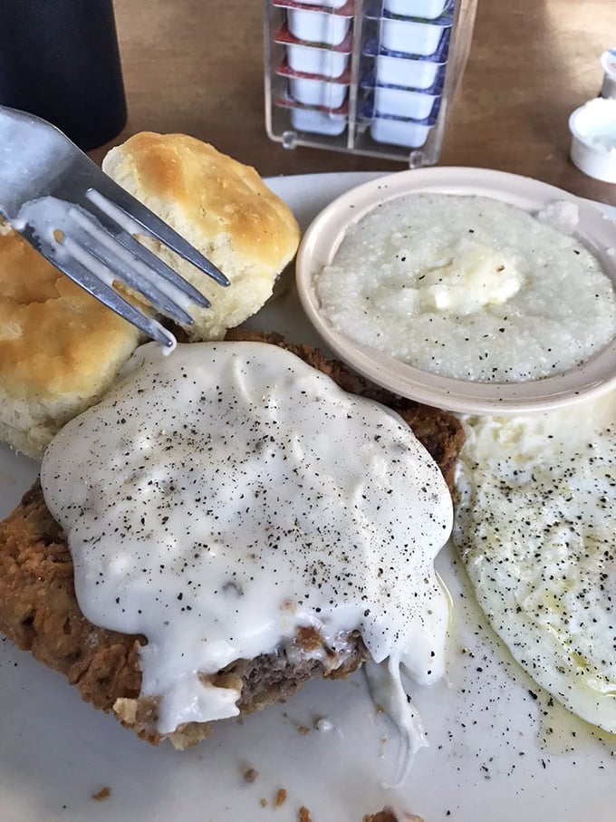Country fried steak smothered in pepper-flecked gravy alongside fluffy biscuits and creamy grits—this is what breakfast dreams are made of.