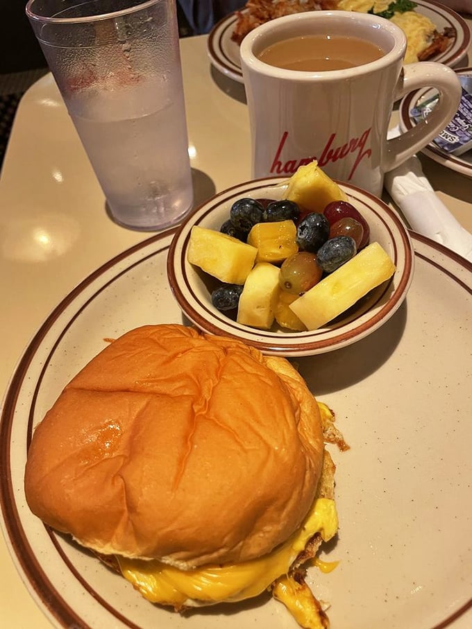 Breakfast sandwich perfection with a side of fresh fruit that technically makes this health food. The golden bun and melty cheese create the morning motivation you didn't know you needed.