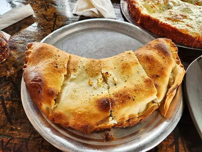 This isn't just a calzone – it's a golden-brown fortress protecting a treasure trove of cheese and fillings that's worth storming the castle for.