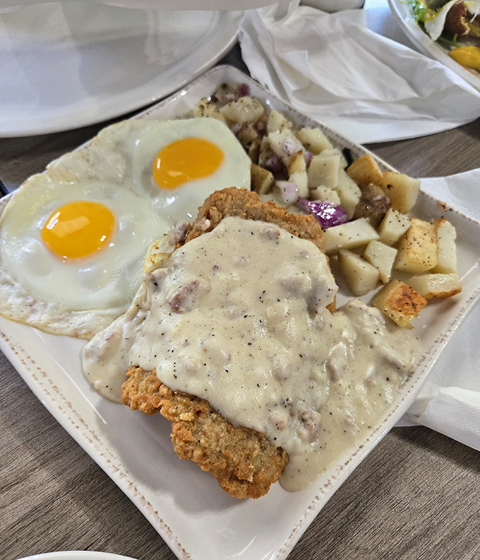 The legendary chicken fried steak in all its glory – golden crispy exterior, smothered in peppery gravy, with sunny-side eggs standing guard. This is breakfast nirvana.