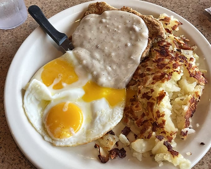 Country fried steak crowned with pepper-flecked gravy alongside sunny-side eggs and golden hash browns—the breakfast trinity that launches a thousand great days.