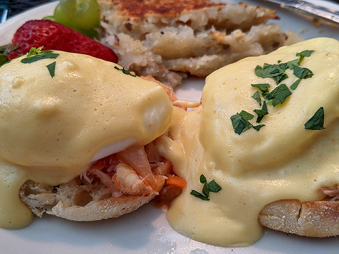 Hollandaise sauce cascades like golden velvet over these eggs Benedict, with each poached egg perched perfectly atop what appears to be seafood.