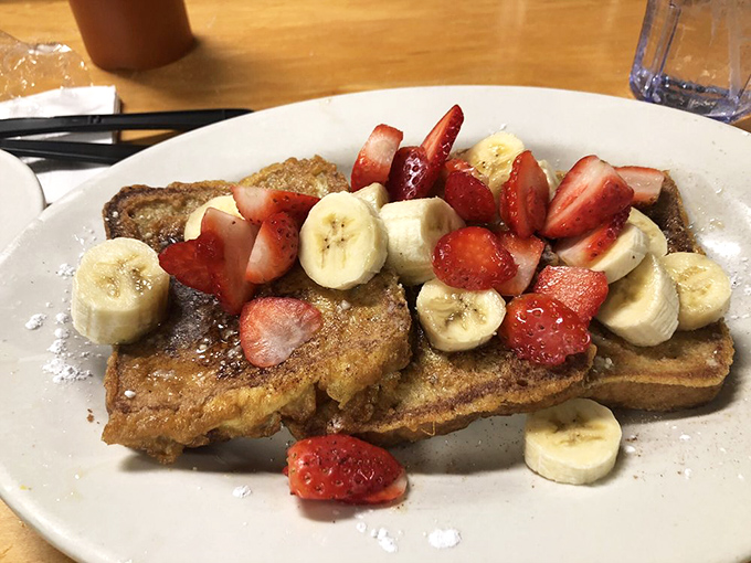 French toast that doesn't just arrive—it makes an entrance, crowned with fresh strawberries and bananas like breakfast royalty.