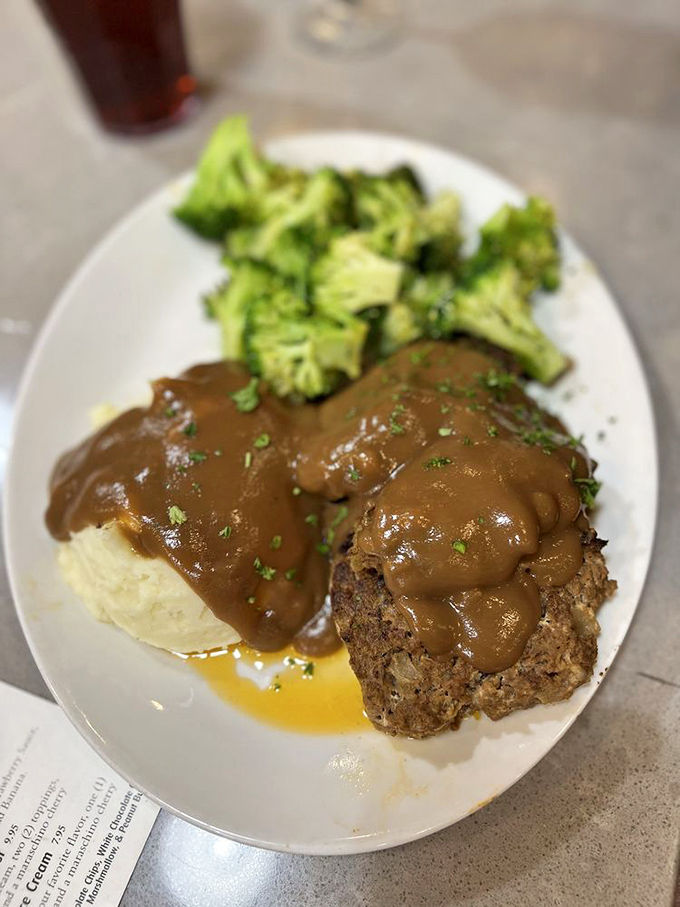 The star of the show arrives: meatloaf draped in rich gravy alongside bright broccoli—proof that sometimes the simplest dishes make the most profound statements.