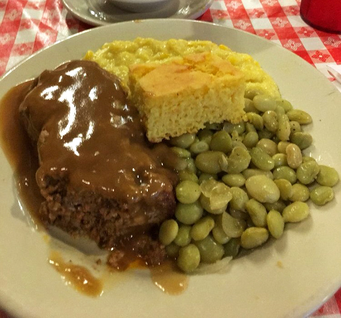 Behold the star attraction: meatloaf bathed in rich gravy alongside cornbread and lima beans—a plate that could make a vegetarian reconsider their life choices.