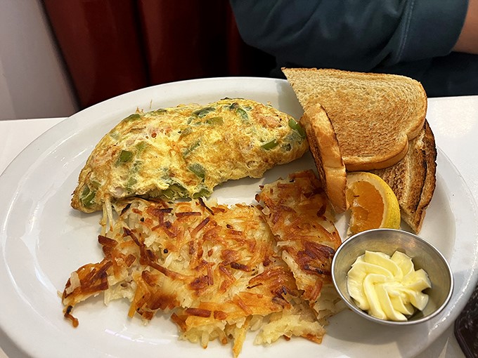 This omelet doesn't just arrive at your table—it makes an entrance, flanked by crispy hash browns that audition for the role of breakfast's best supporting actor.