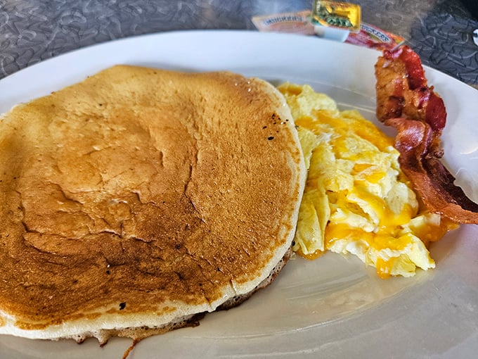 One perfect pancake, eggs with cheese melting like sunshine, and bacon crisp enough to snap – the holy trinity of diner breakfast done right.