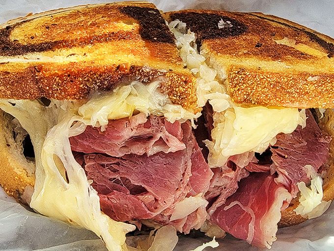 Behold the Reuben in its natural habitat – perfectly grilled marble rye embracing a mountain of corned beef, sauerkraut, and Swiss cheese in perfect harmony.