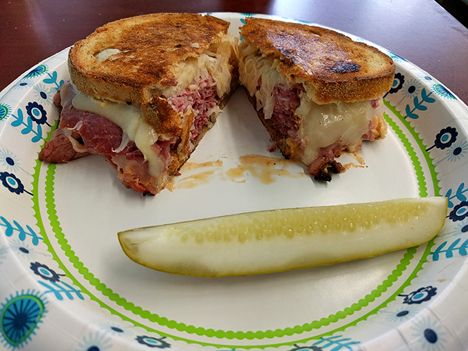 Behold the Reuben in its natural habitat—perfectly grilled, gloriously melty, and accompanied by its faithful sidekick, the pickle spear.