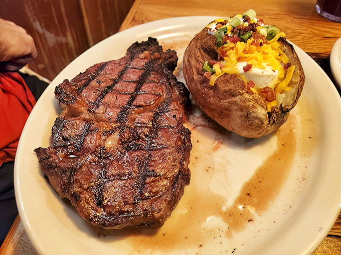 A ribeye with perfect grill marks alongside a loaded baked potato. This isn't just dinner—it's a religious experience for carnivores.