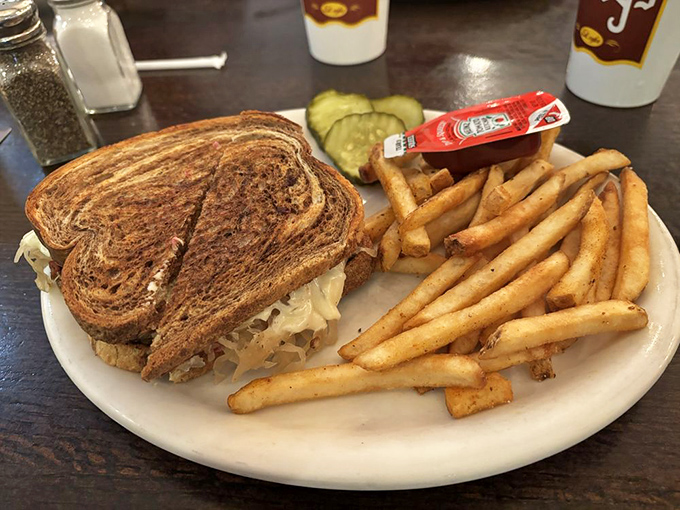 The legendary Reuben in its natural habitat – perfectly grilled rye bread embracing a mountain of corned beef, with golden fries standing guard.