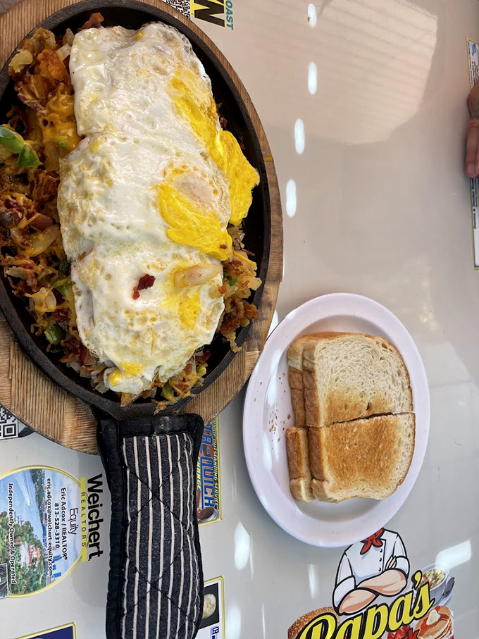 Breakfast nirvana on a sizzling skillet—eggs lounging atop a mountain of hash browns and fixings, with toast standing by for dipping duty.