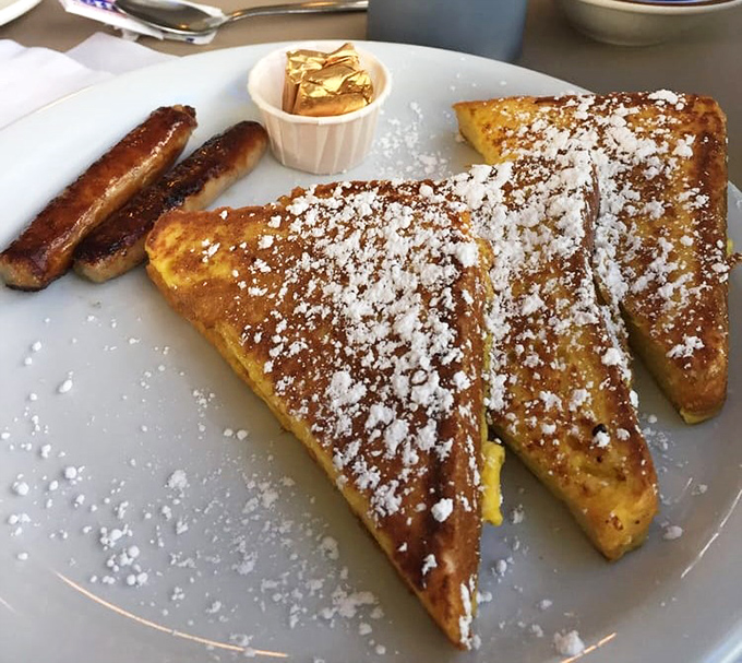 Golden-brown French toast dusted with powdered sugar sits alongside perfectly caramelized sausage links—breakfast nirvana on a plate.