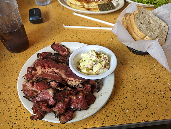 Pastrami so tender it practically surrenders to your fork, accompanied by that legendary potato salad—a side dish that refuses to be upstaged.