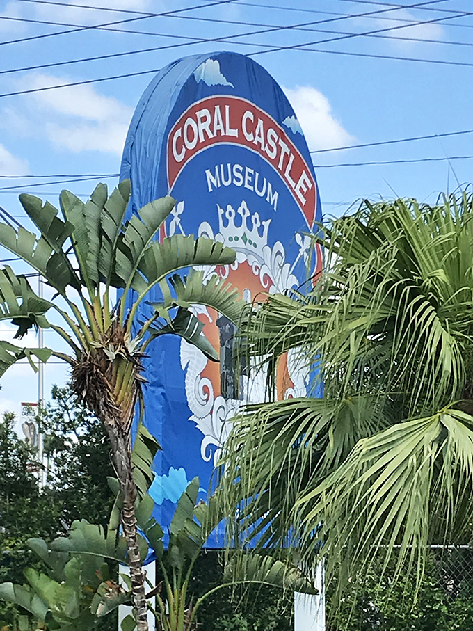 The colorful Coral Castle Museum sign stands tall among tropical palms, like a cheerful sentinel guarding Florida's most puzzling attraction.