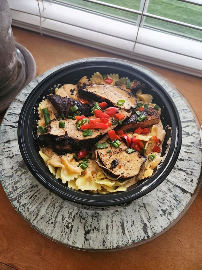 Blackened chicken atop bowtie pasta, garnished with fresh peppers and herbs – proof that paradise can indeed be found in a takeout container.