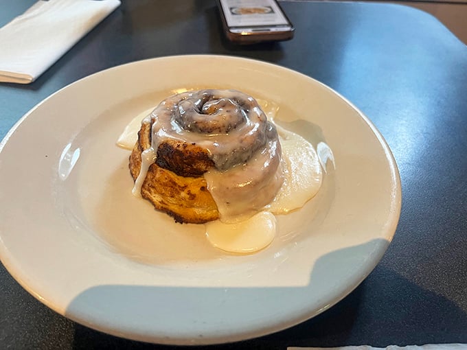 The cinnamon roll arrives like a warm hug on a plate—glistening, spiraled, and demanding to be the center of attention.
