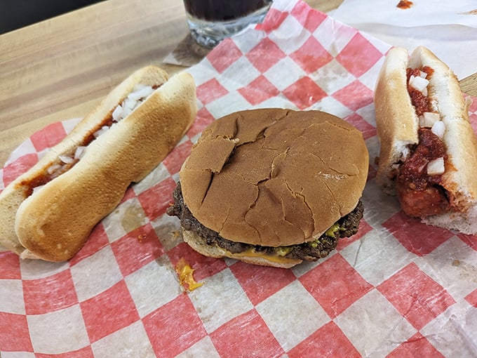 The holy trinity of Michigan roadside dining: a classic cheeseburger flanked by two coney dogs, all served on checkered paper—nature's perfect meal doesn't need fancy plating.
