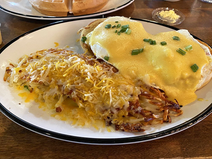 Eggs Benedict with crispy hashbrowns—where hollandaise sauce cascades down like a yellow waterfall of buttery goodness that dreams are made of.