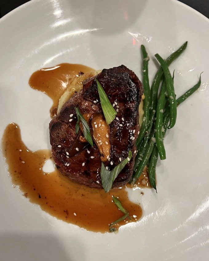 Behold the filet mignon in its natural habitat: perfectly seared, adorned with green onions and sesame seeds, lounging in a sauce worth bottling.