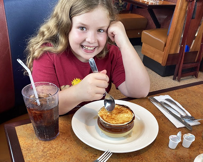 A young diner enjoys the simple pleasure of French onion soup, proving that comfort food appreciation starts early in Pennsylvania.