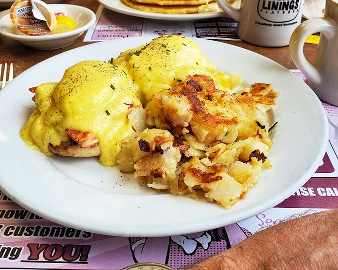 Eggs Benedict reimagined—golden hollandaise cascading over perfectly poached eggs like a breakfast waterfall, with home fries that demand equal attention. 