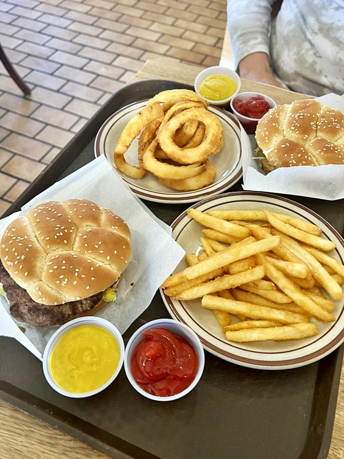 The holy trinity of comfort: golden onion rings, crispy fries, and burgers on paper—proof that sometimes the simplest pleasures are the most profound.