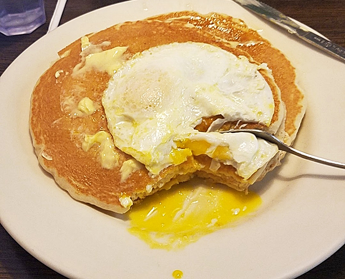 Breakfast architecture at its finest—a sunny-side-up egg crowning a pancake throne. The yolk breaks like sunrise over a carb horizon.