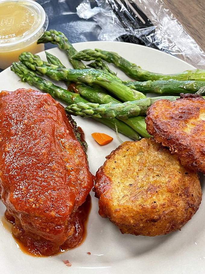 The meatloaf's tomato-glazed crown jewel sits alongside perfectly roasted potato pancakes and fresh asparagus—proof that simple food done right is culinary royalty.