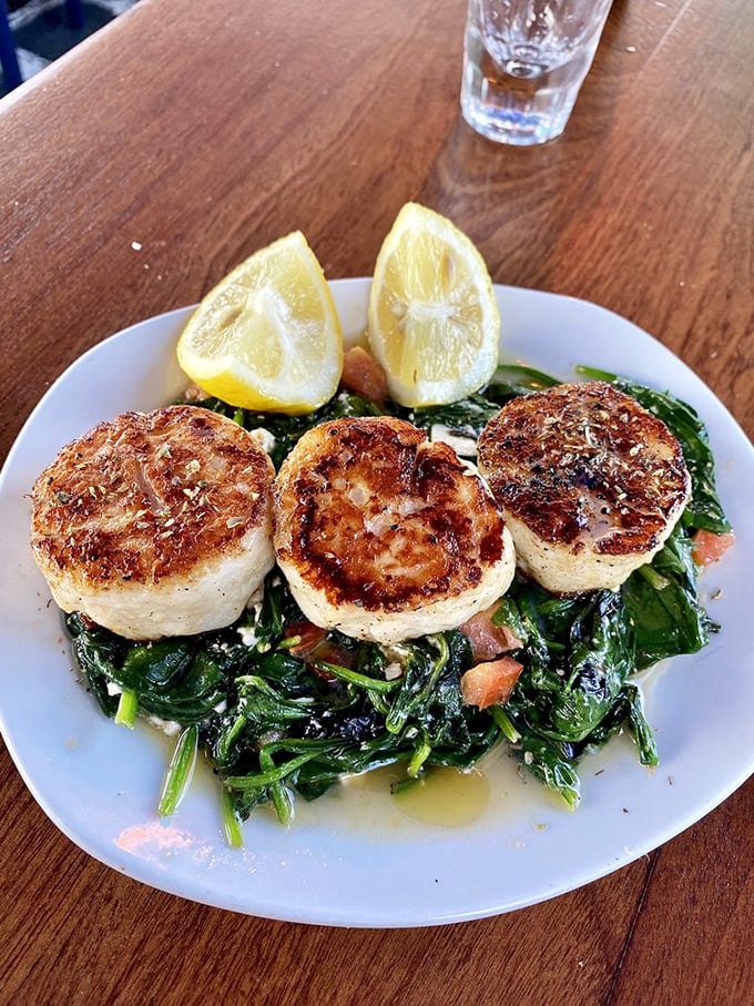 Perfectly seared scallops lounging on a bed of sautéed greens. A trio of ocean sweetness with lemon wedges standing by for duty.